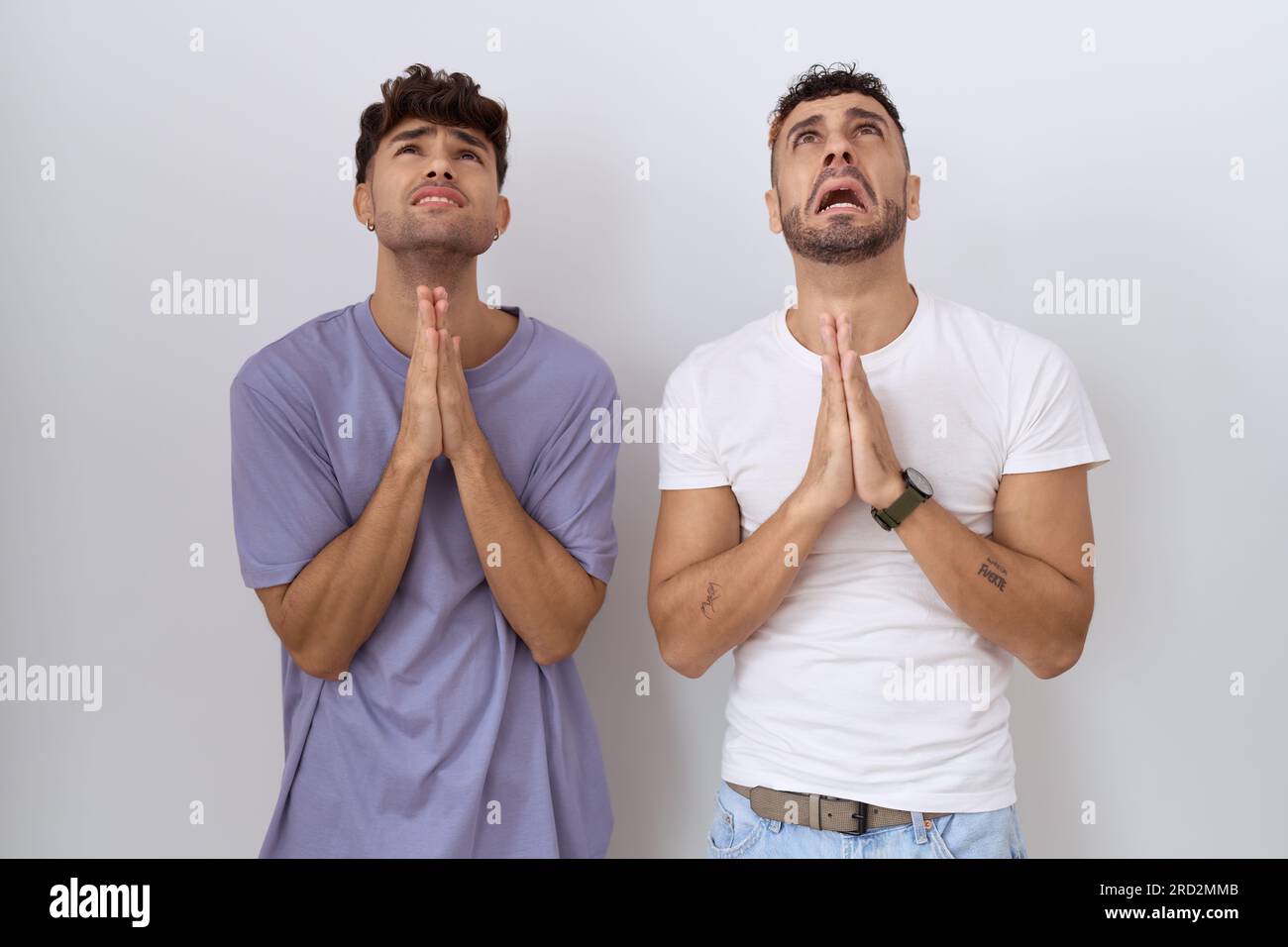 Homosexual gay couple standing over white background begging and ...