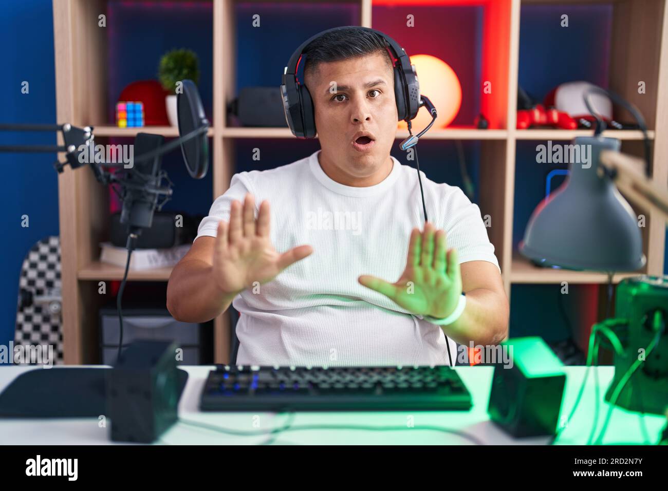 Young hispanic man playing video games moving away hands palms showing ...