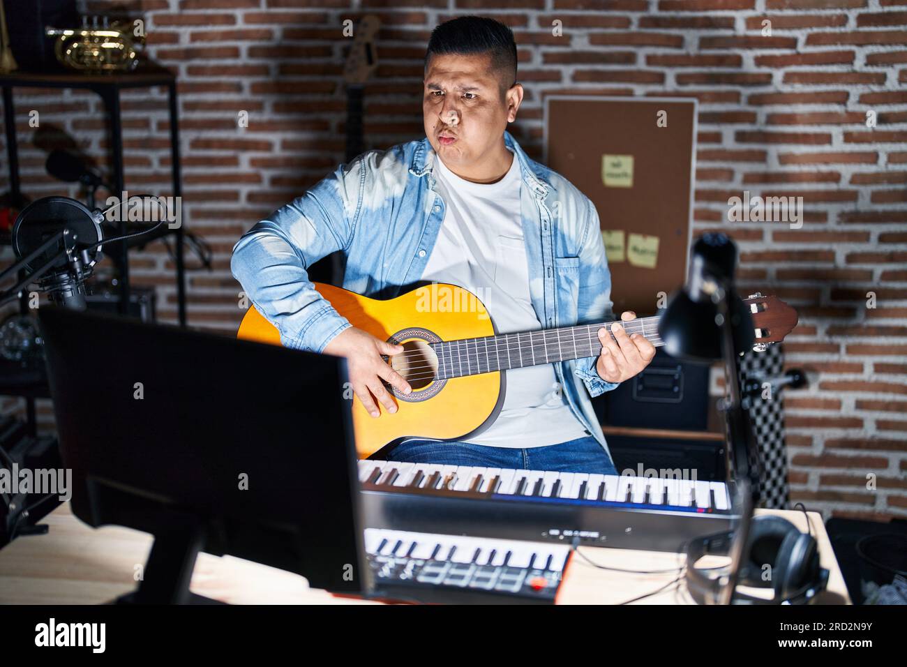 Hispanic young man playing classic guitar at music studio puffing ...