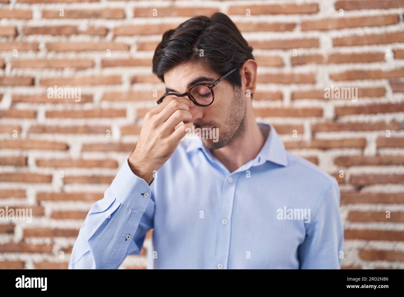 Young hispanic man standing over brick wall background tired rubbing ...