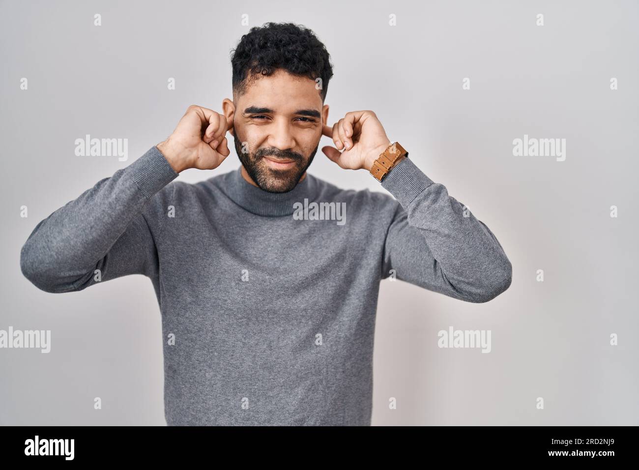 Hispanic man with beard standing over white background covering ears ...