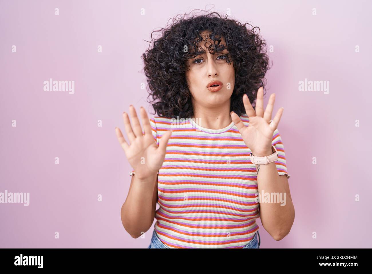 Young middle east woman standing over pink background moving away hands ...