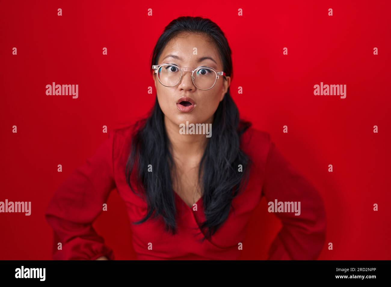 Asian young woman standing over red background afraid and shocked with ...