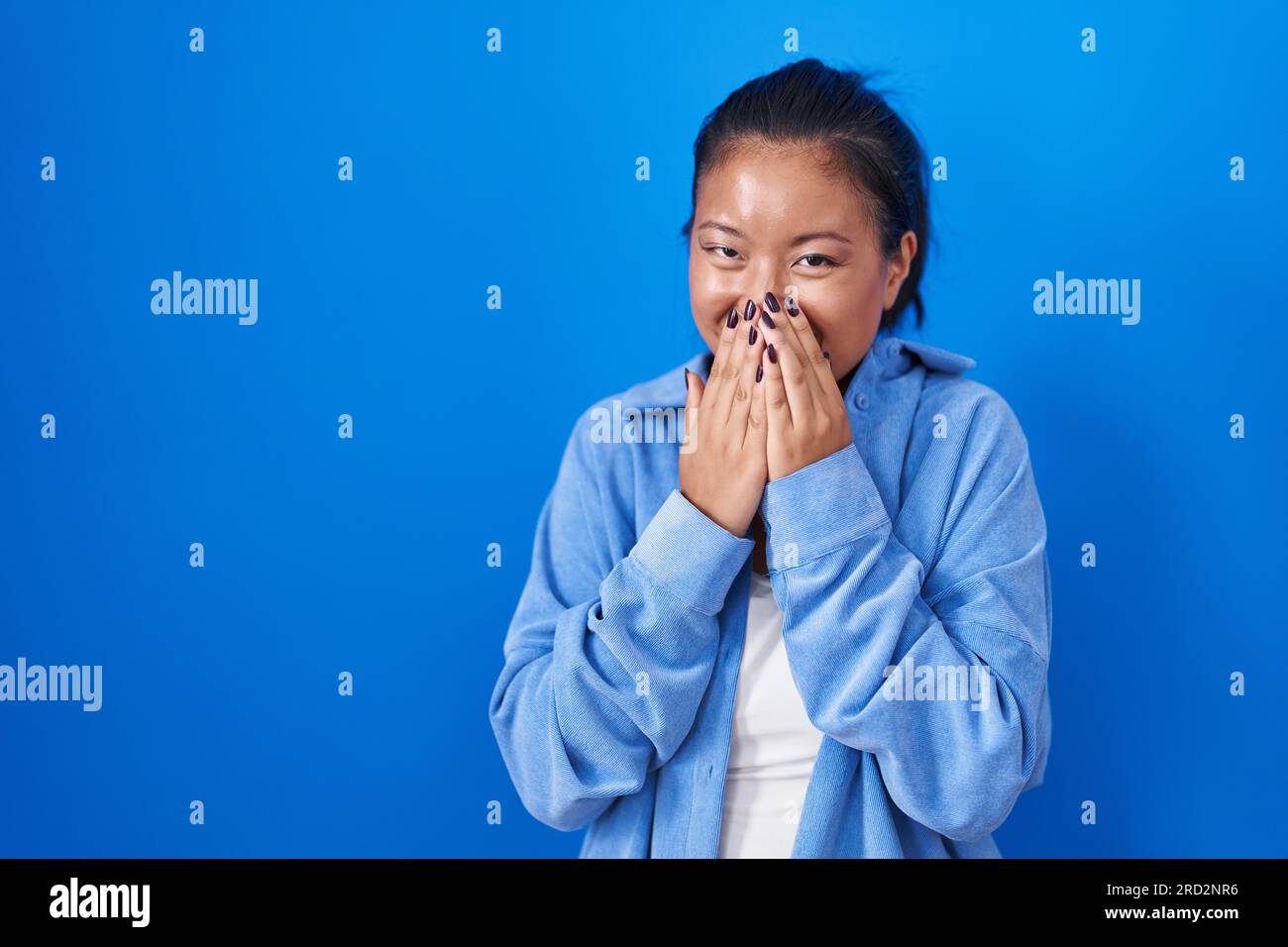 Asian young woman standing over blue background laughing and ...