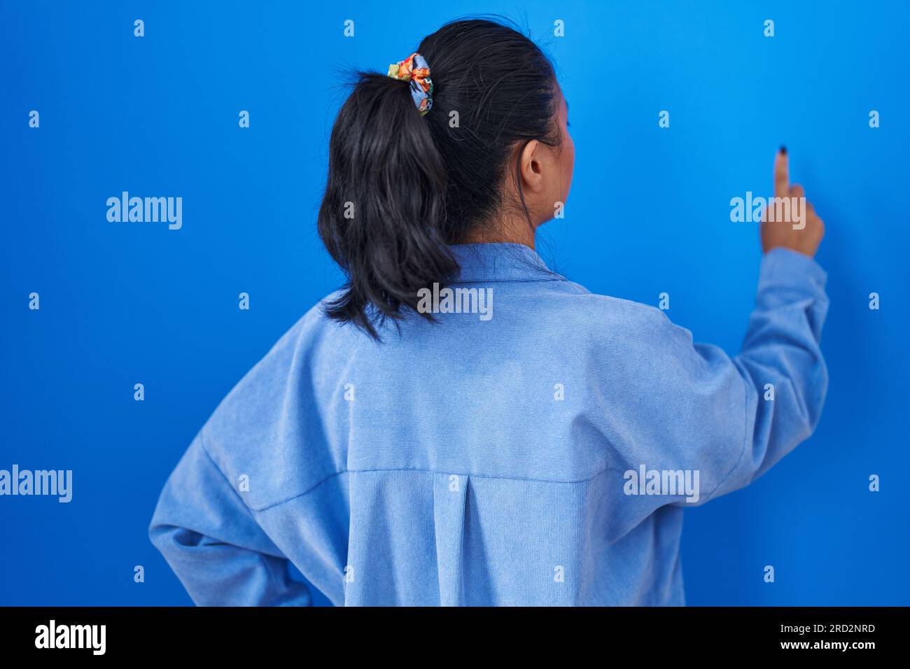 Asian young woman standing over blue background posing backwards ...