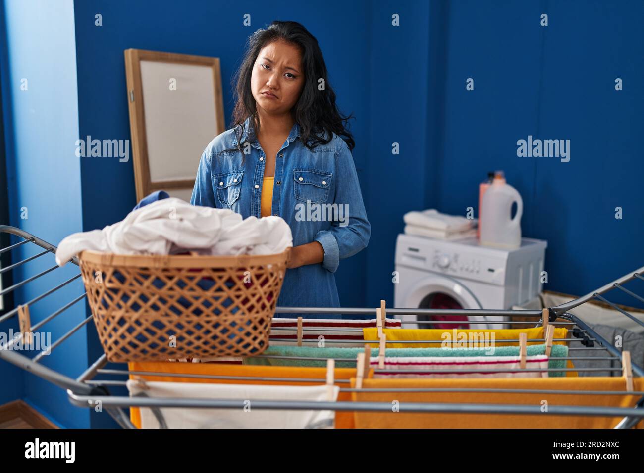 Young asian woman hanging clothes at clothesline depressed and worry ...