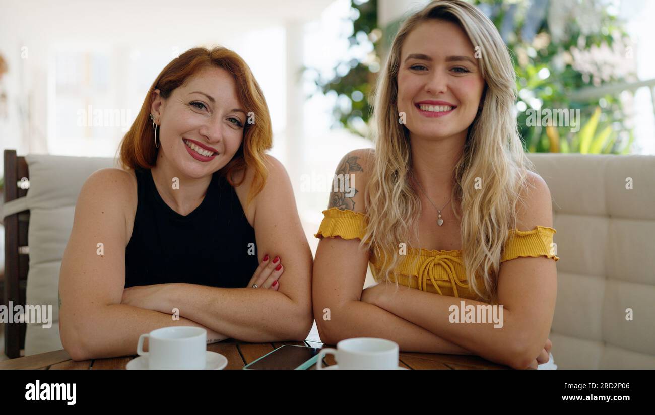 Two women drinking coffee sitting on table with arms crossed gesture at ...