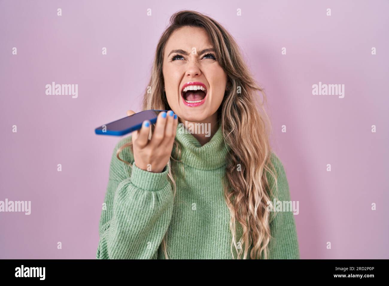 Young caucasian woman sending a voice message with smartphone angry and ...