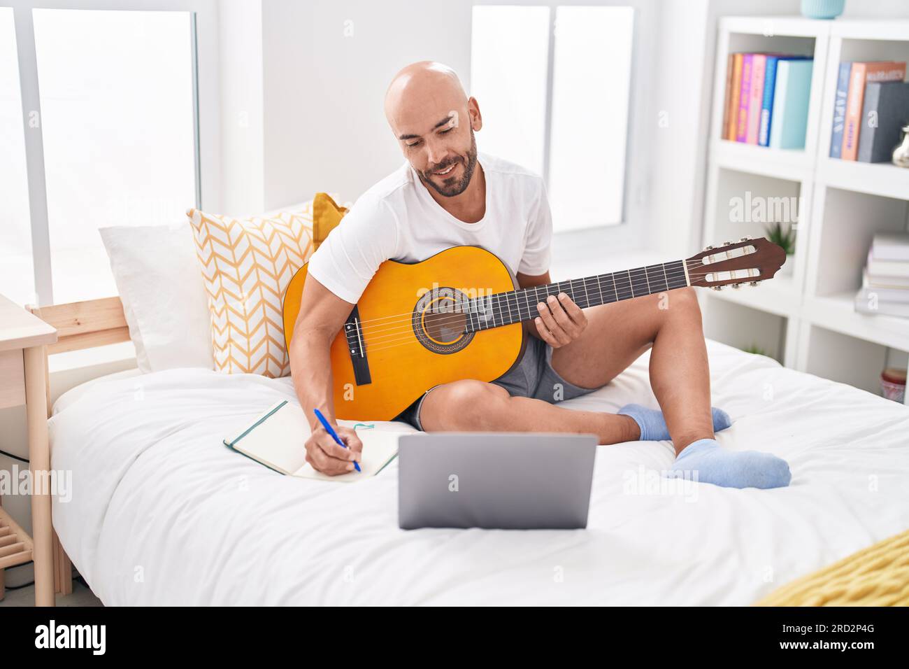 Young bald man composing song playing classical guitar sitting on bed ... Young bald man composing song playing classical guitar sitting on bed ...