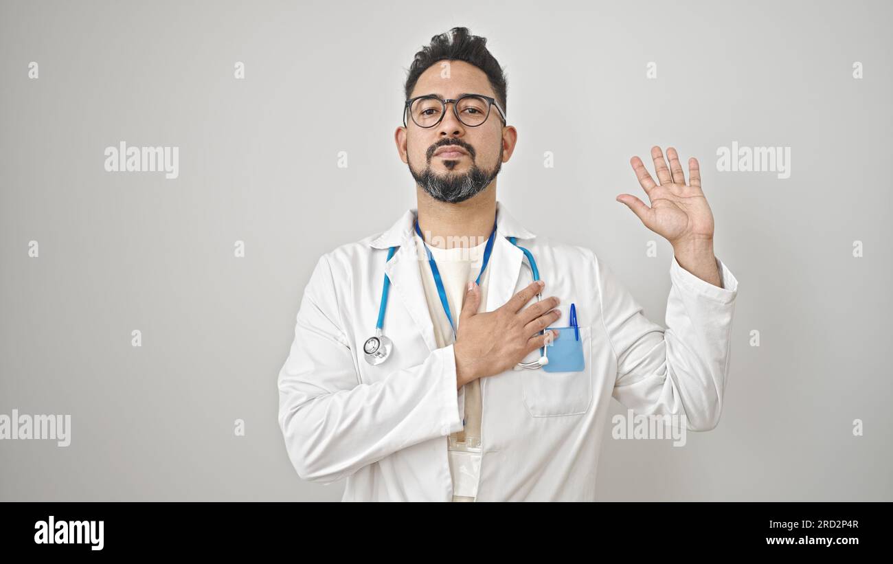 Young latin man doctor making an oath with hand on chest over isolated ...