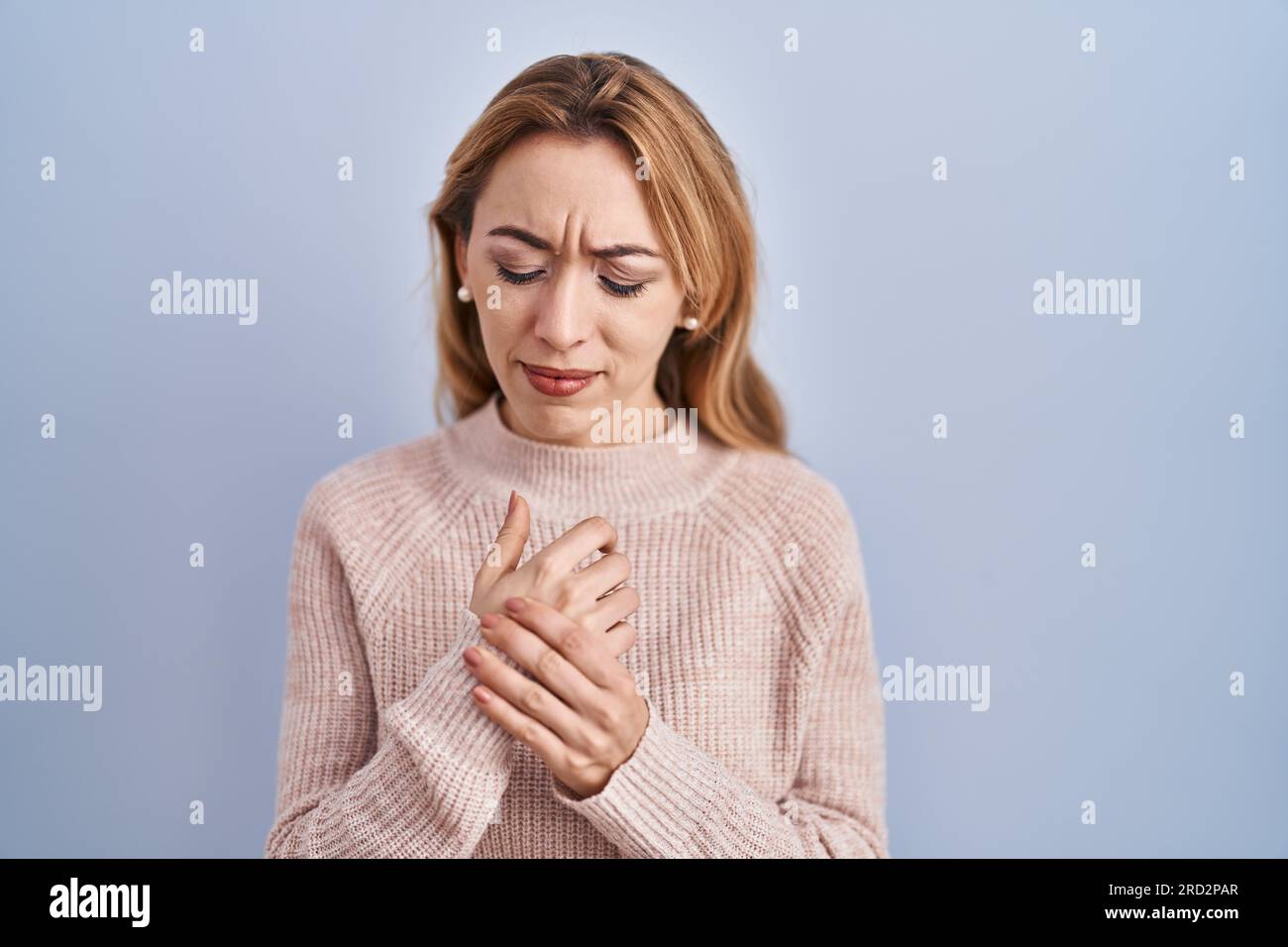Hispanic woman standing over blue background suffering pain on hands ...