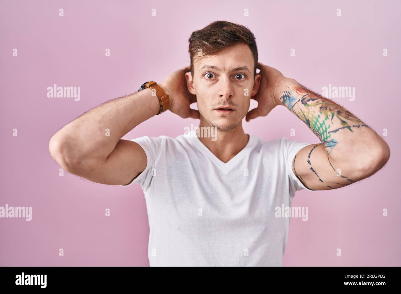 Caucasian man standing over pink background crazy and scared with hands ...