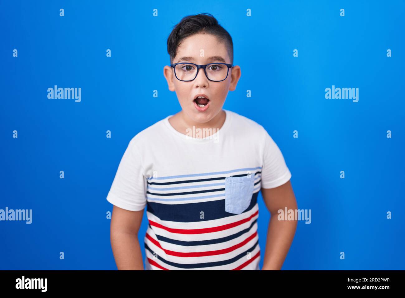 Young hispanic kid standing over blue background afraid and shocked ...