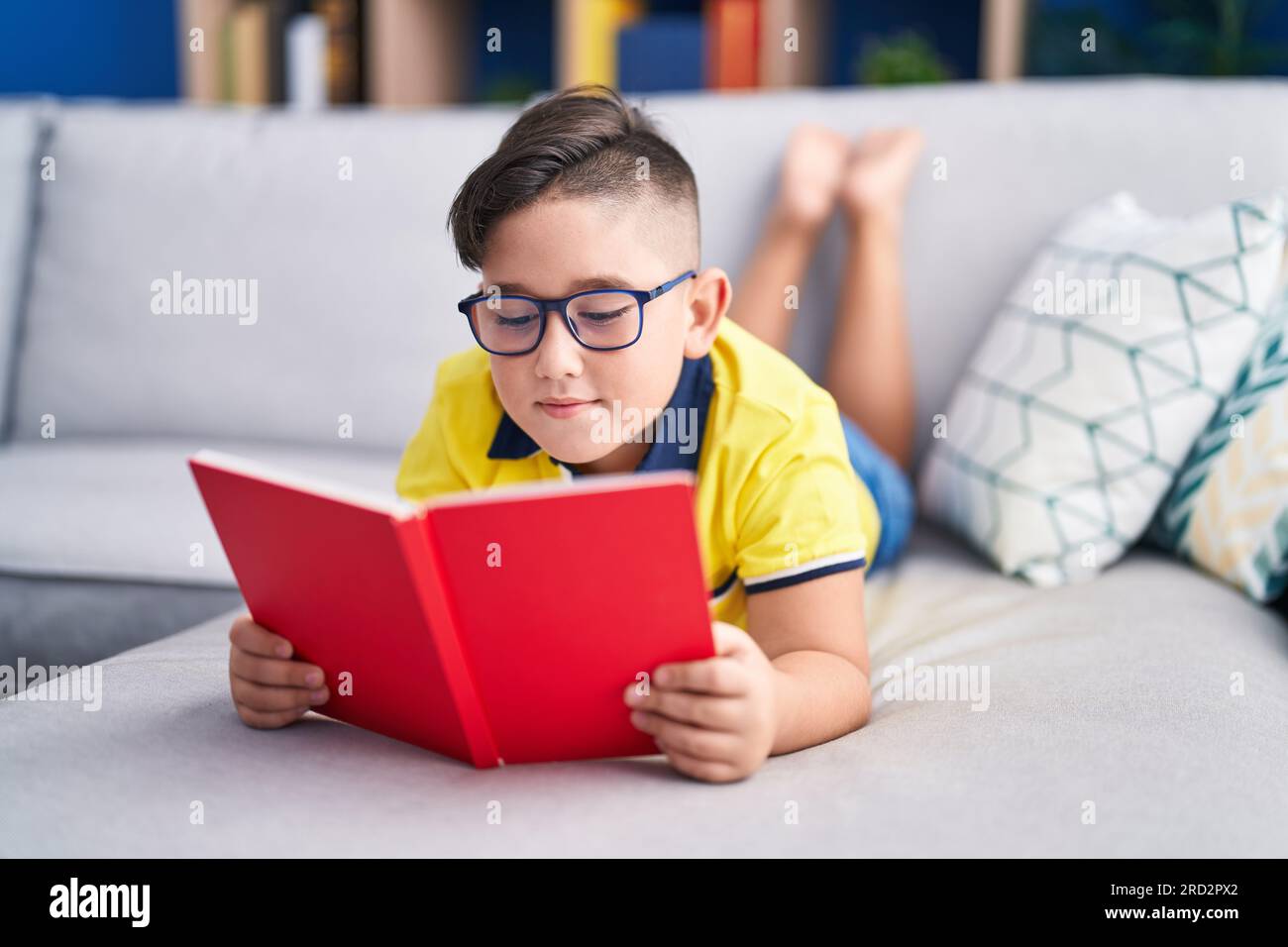 Adorable hispanic boy reading book lying on sofa at home Stock Photo ...