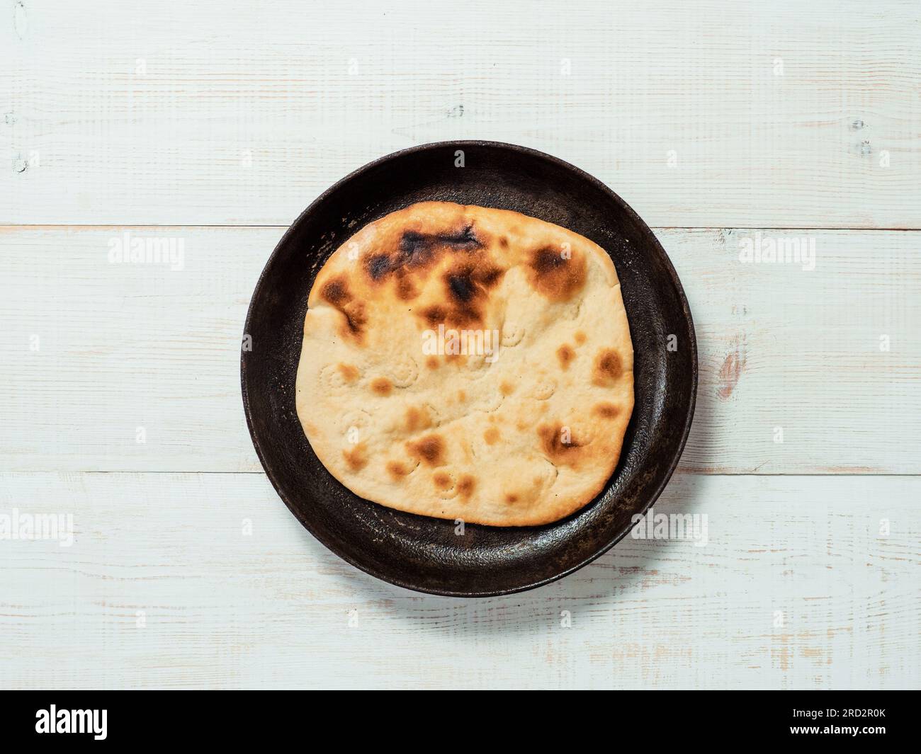 Fresh naan bread in cast-iron pan on white wooden background with copy ...