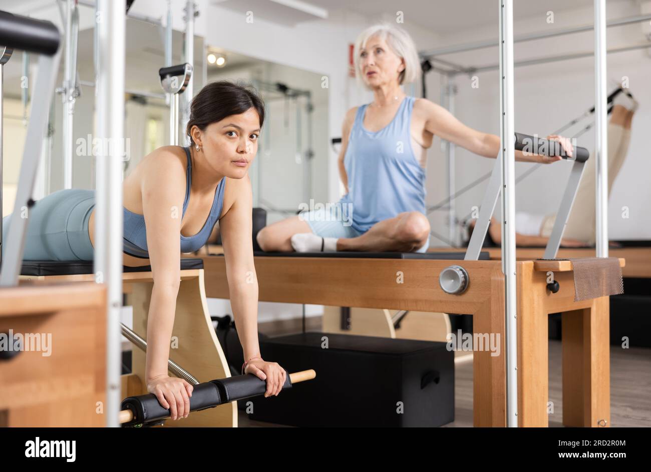 Focused woman performing set of pilates exercises on reformer in ...