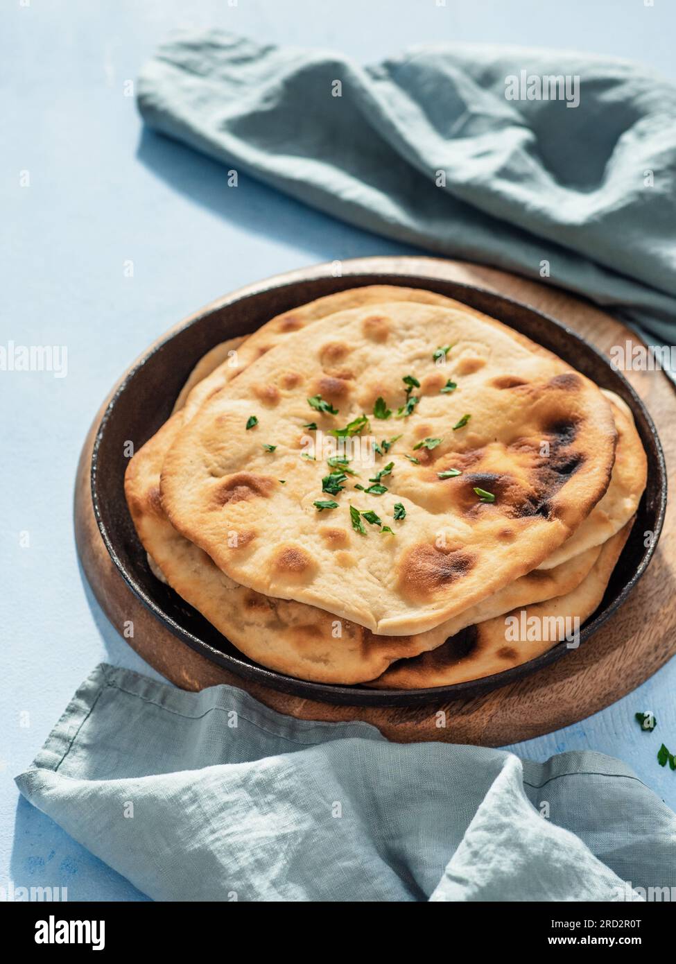 Stack of fesh naan breads in cast-iron pan on blue background with copy ...