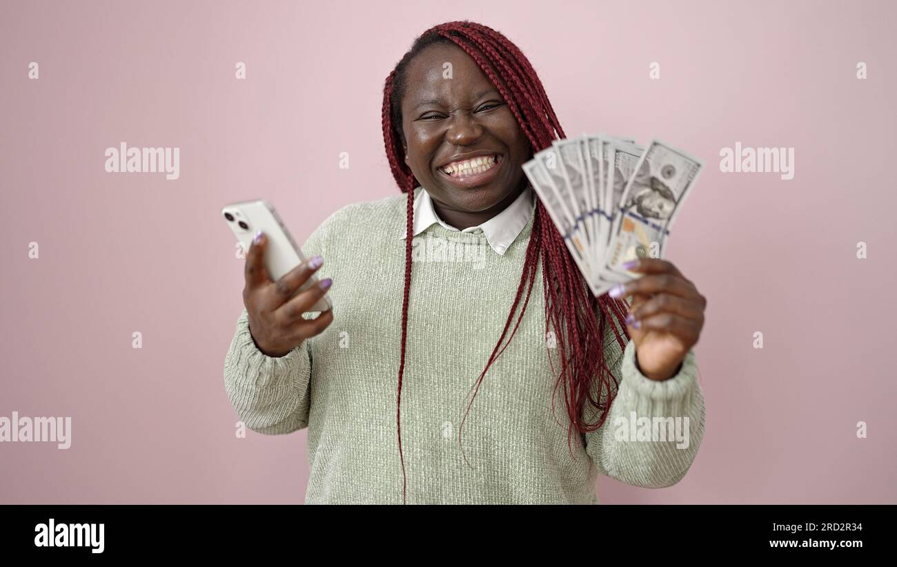 African woman with braided hair smiling holding money and smartphone ...
