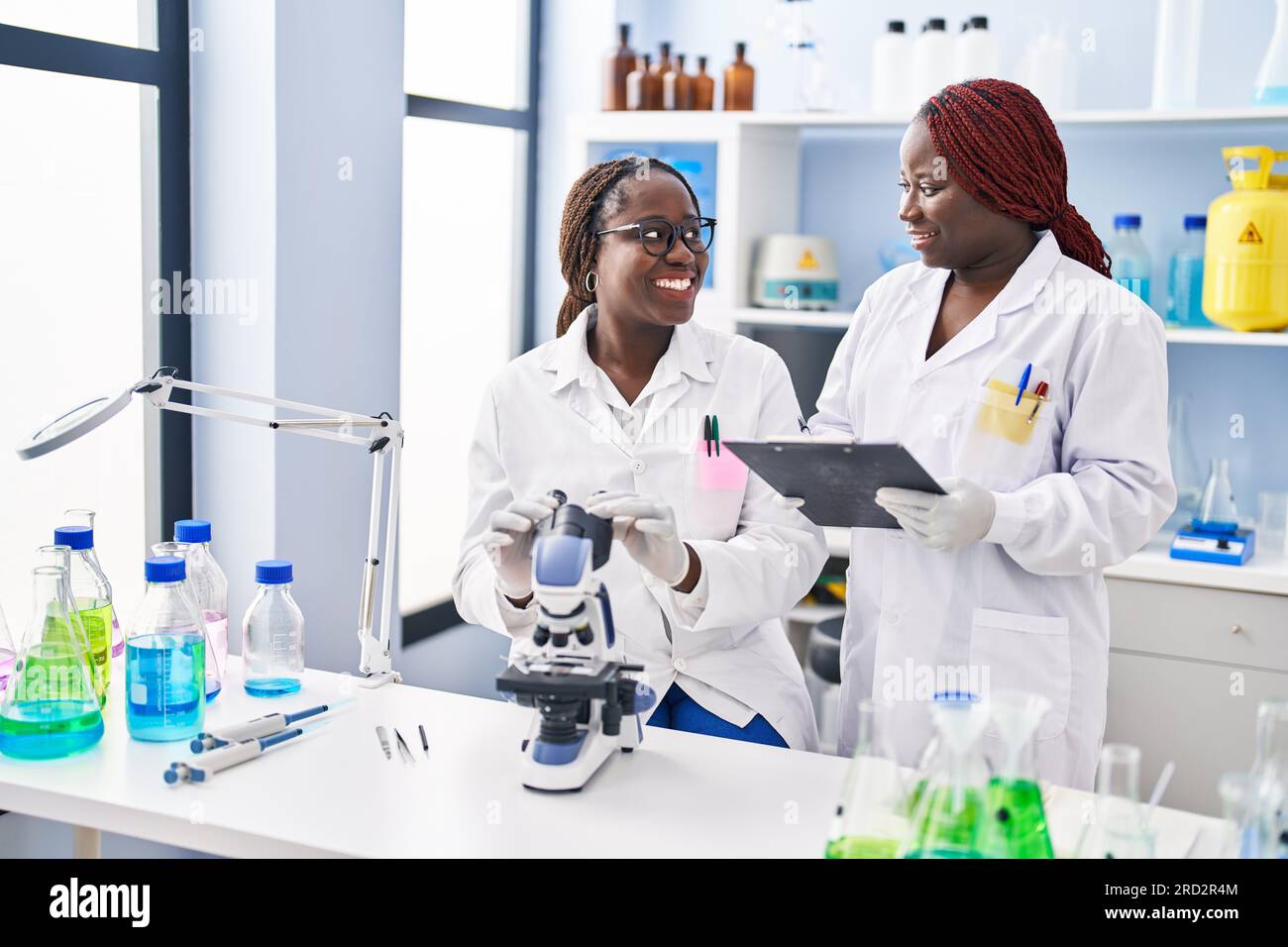 African american women scientists using microscope writing on document at laboratory Stock Photo ...