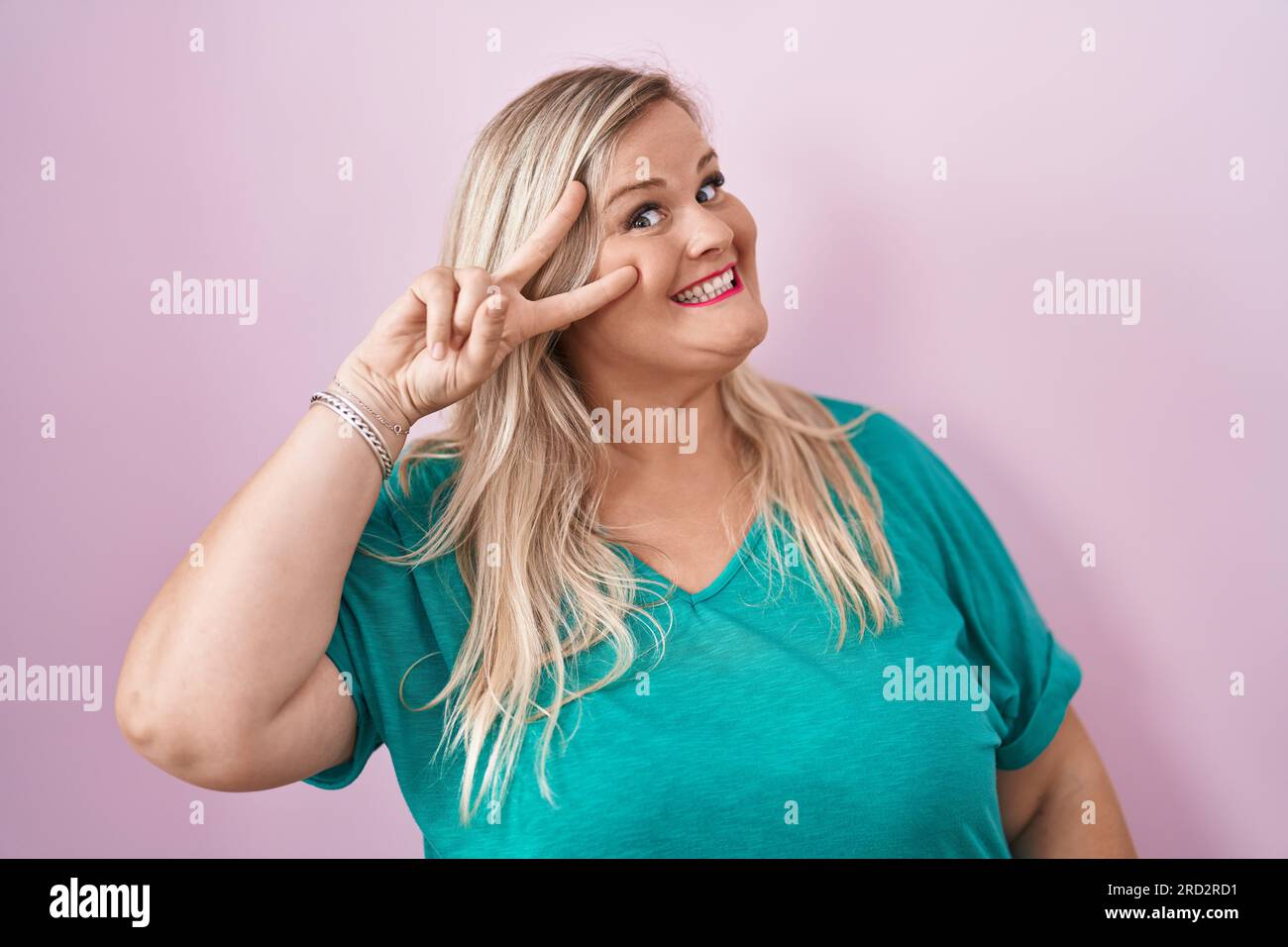 Caucasian plus size woman standing over pink background doing peace ...