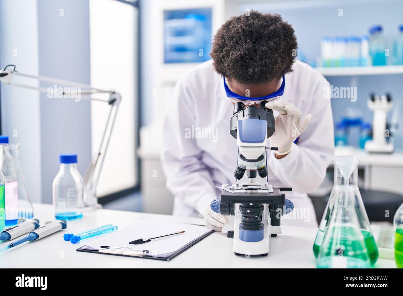 African american woman wearing scientist uniform using microscope at ...