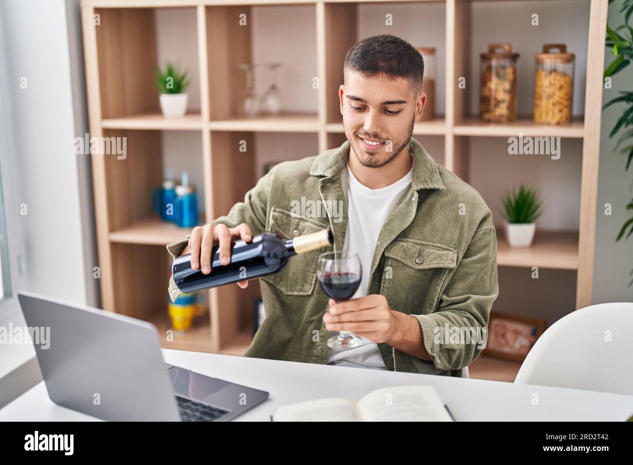 Young hispanic man using laptop pouring wine on glass at home Stock ...