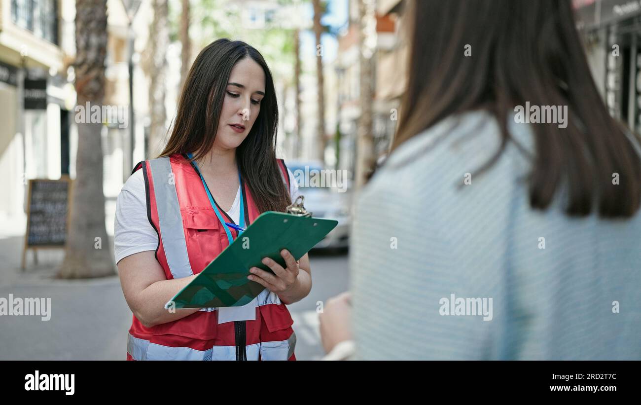 Two women having survey interview writing on clipboard at street Stock ...