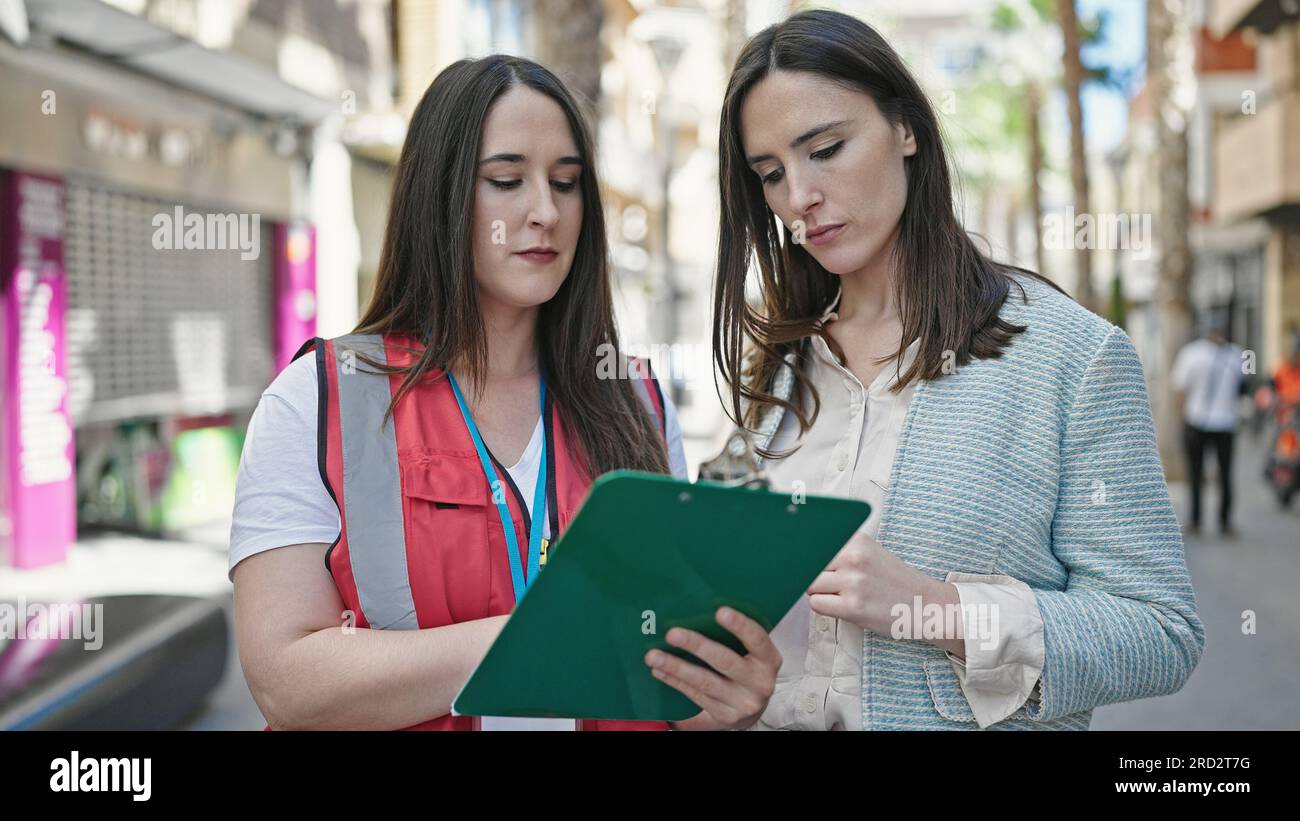 Two women having survey interview writing on clipboard at street Stock ...