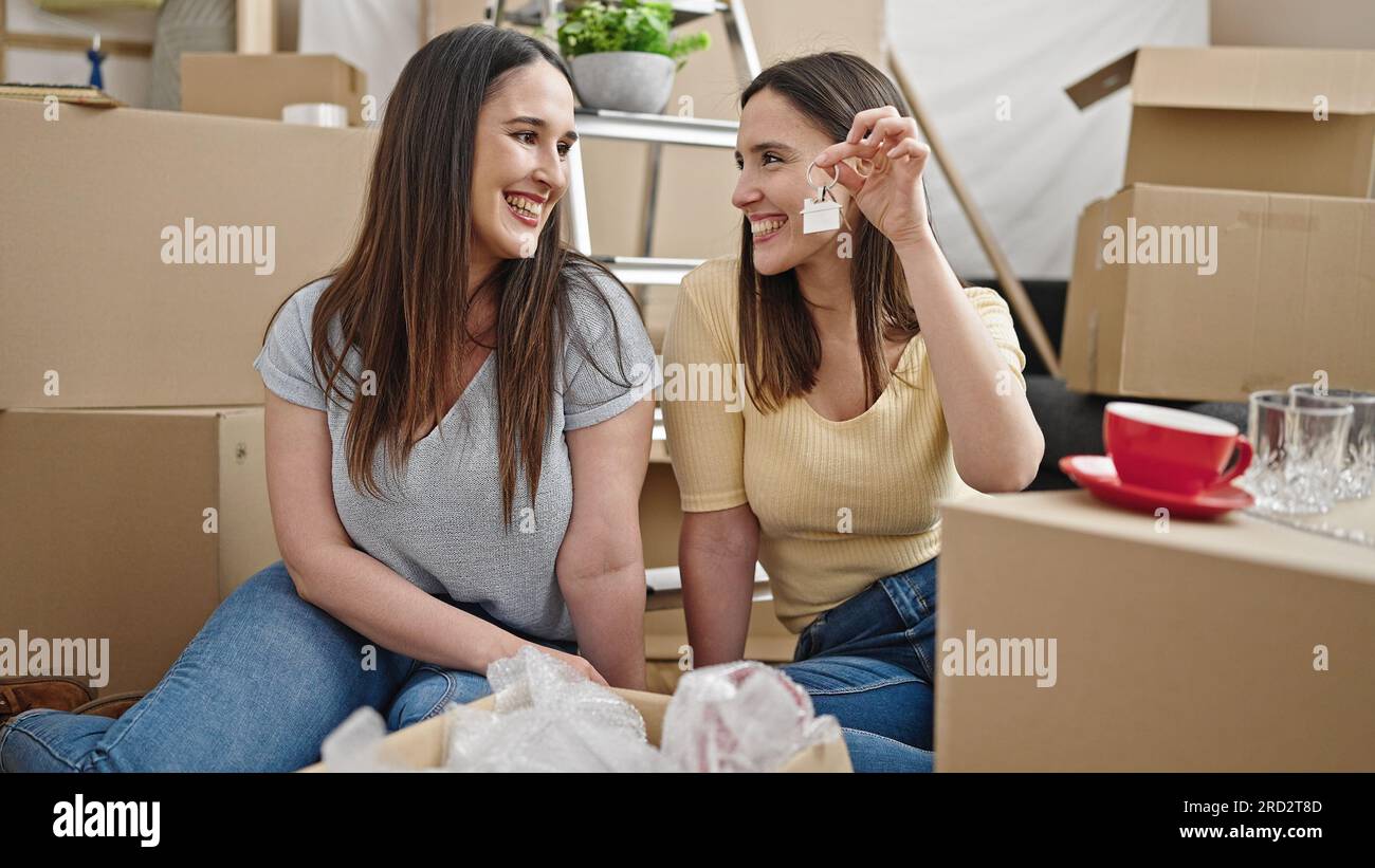 Two women sitting on floor holding keys at new home Stock Photo - Alamy