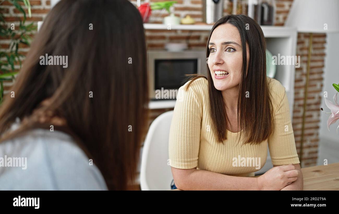Two women sitting on table speaking at dinning room Stock Photo - Alamy