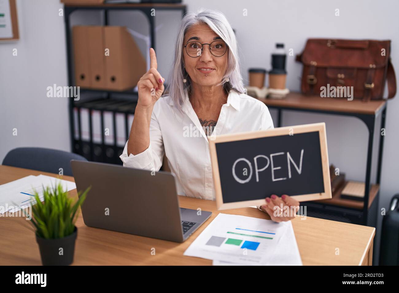 Middle age woman with tattoos at the office holding blackboard with ...