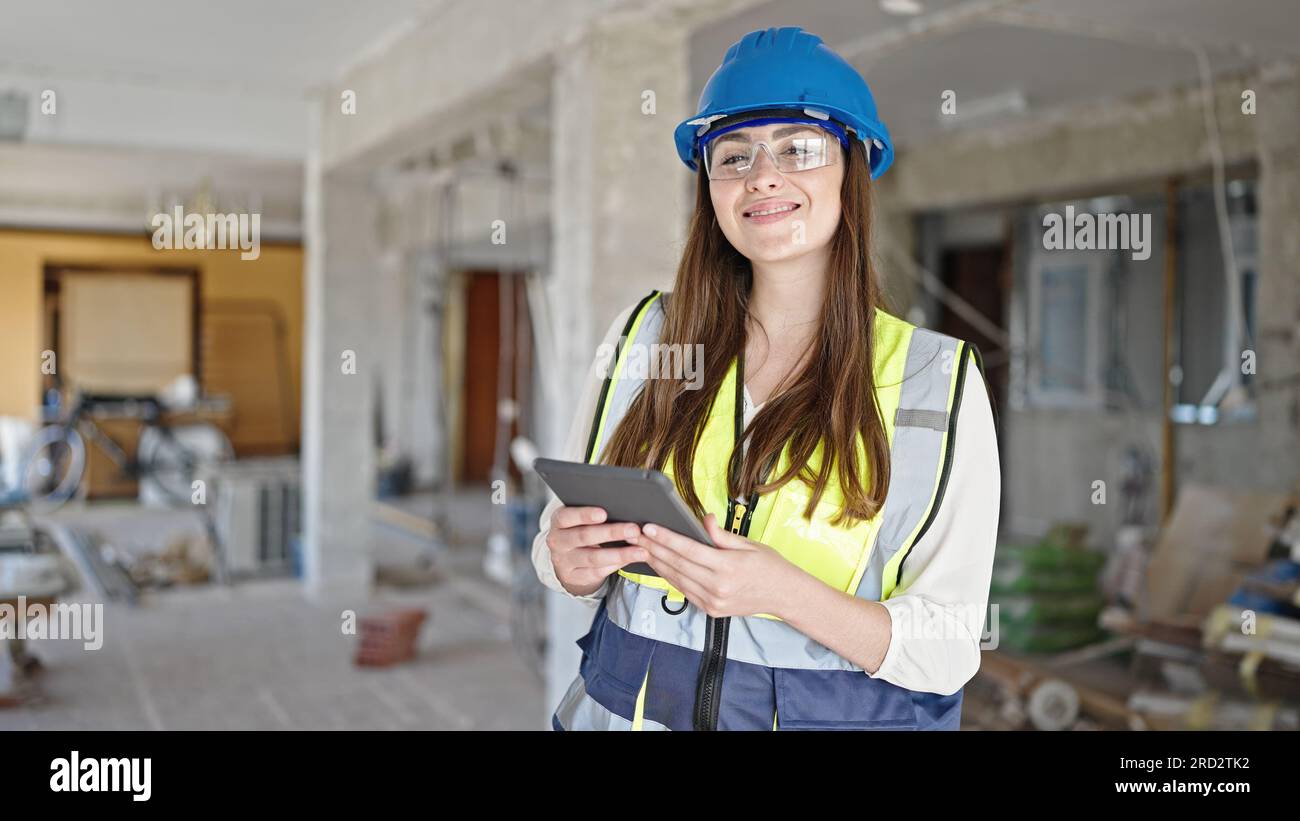 Young beautiful hispanic woman builder using touchpad smiling at ...