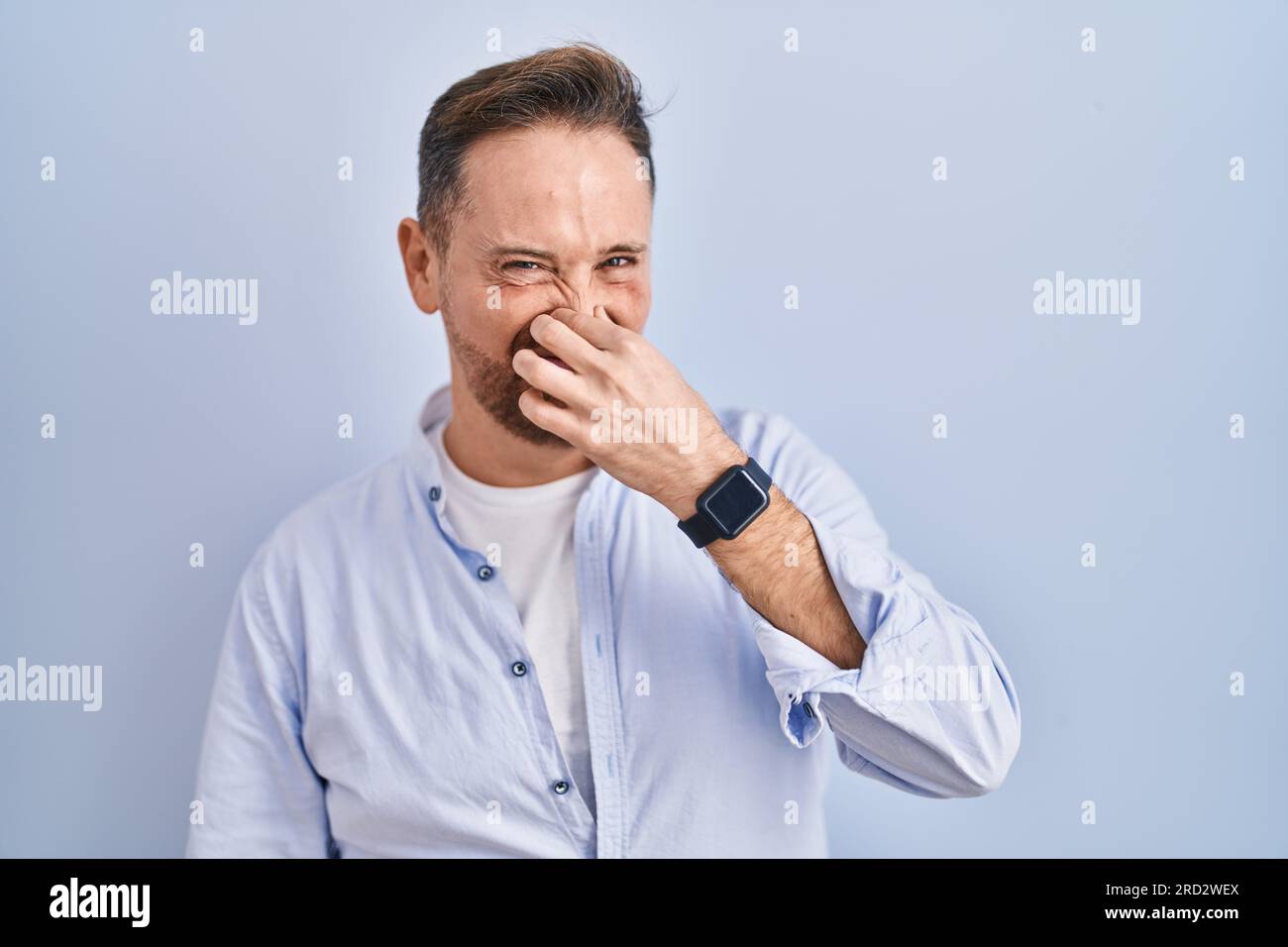 Middle age caucasian man standing over blue background smelling ...