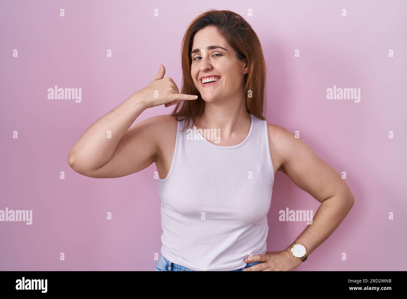 Brunette woman standing over pink background smiling doing phone ...