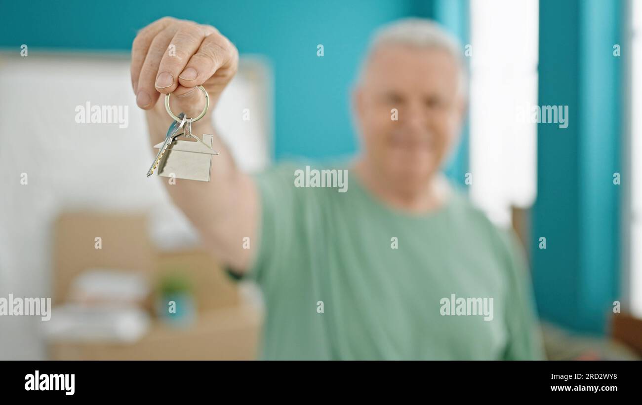 Middle age grey-haired man smiling confident holding keys at new home ...