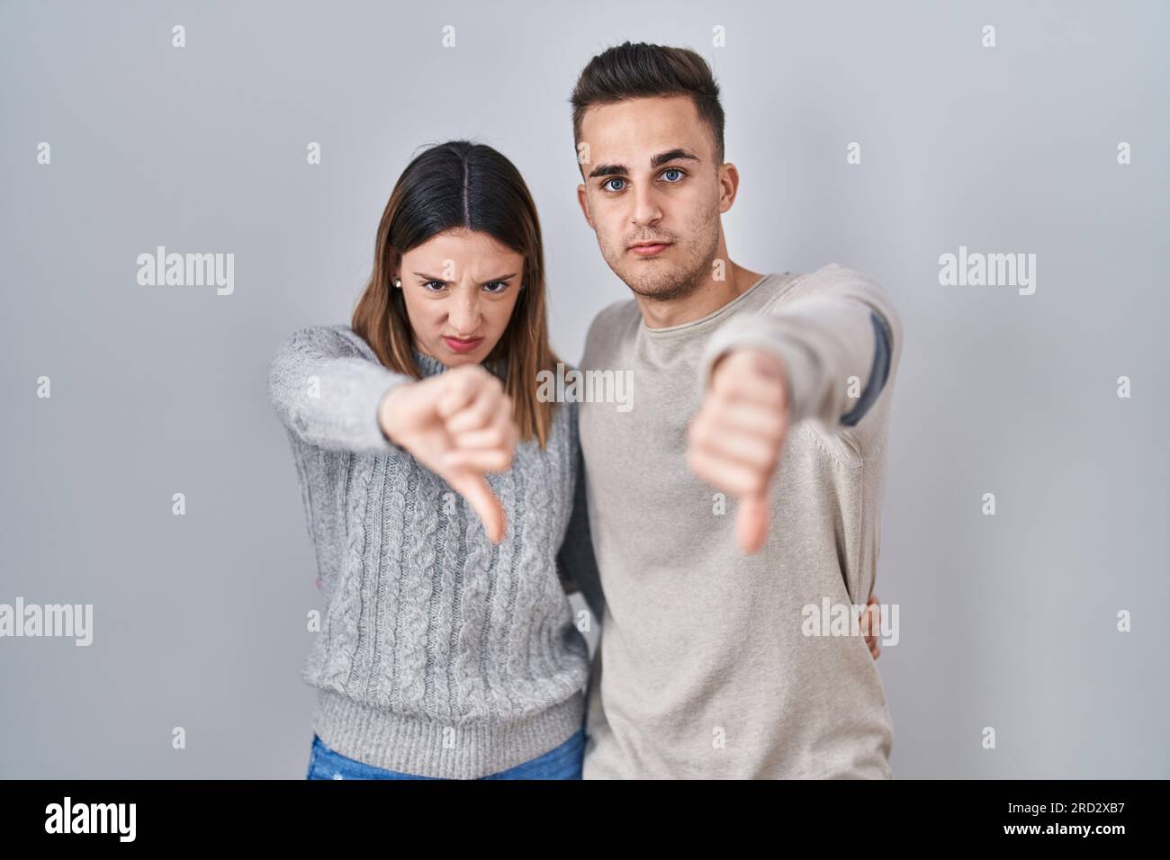 Young hispanic couple standing over white background looking unhappy ...