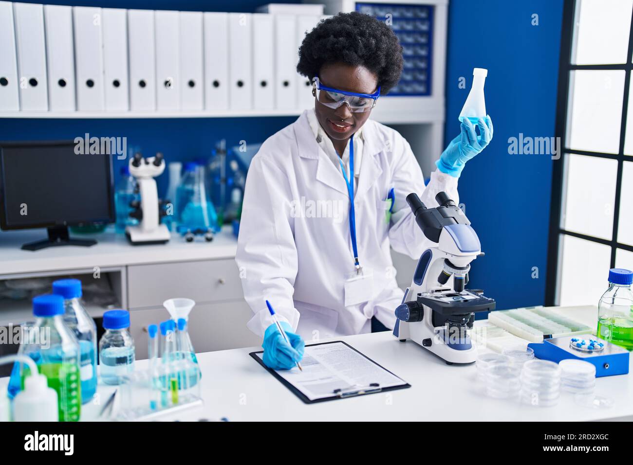 Young african american woman scientist writing on document measuring liquid at laboratory Stock ...