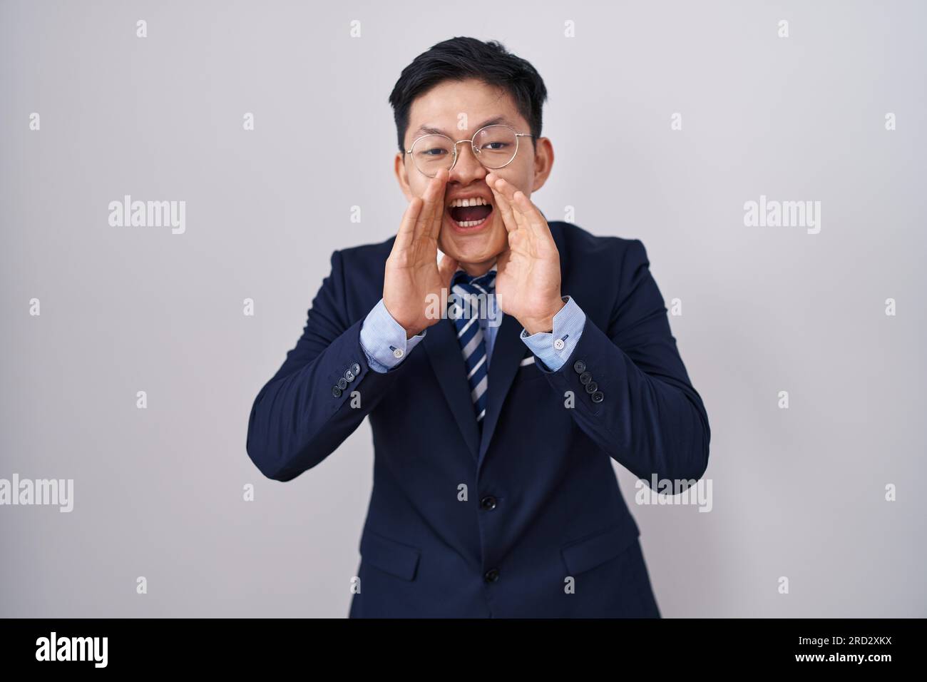 Young asian man wearing business suit and tie shouting angry out loud ...