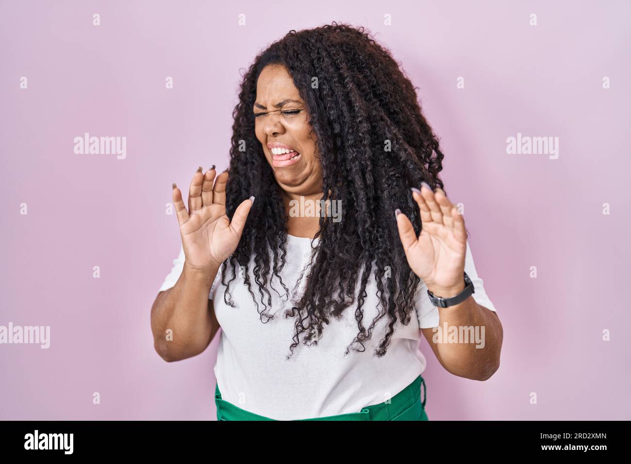 Plus size hispanic woman standing over pink background disgusted ...