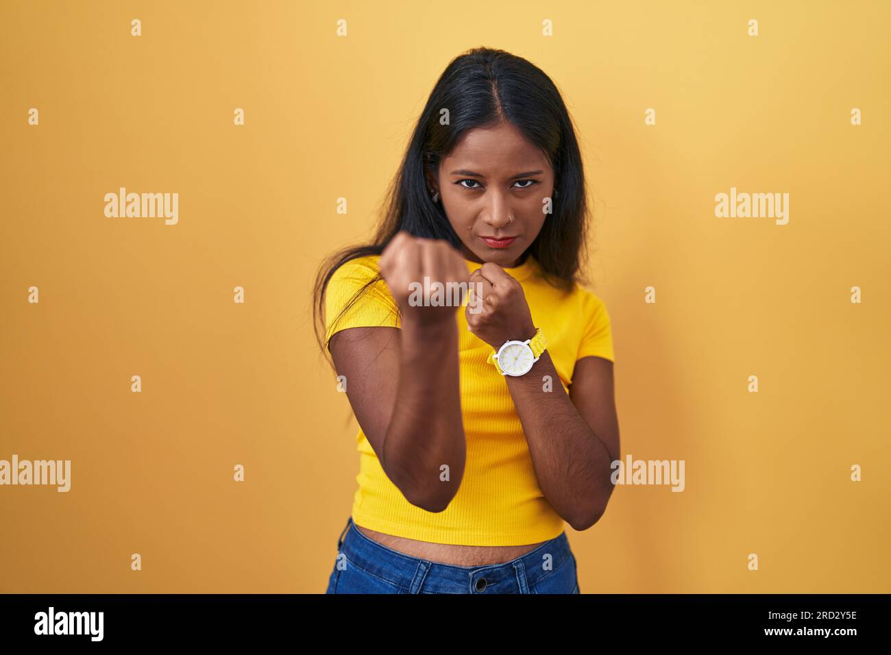 Young indian woman standing over yellow background ready to fight with ...