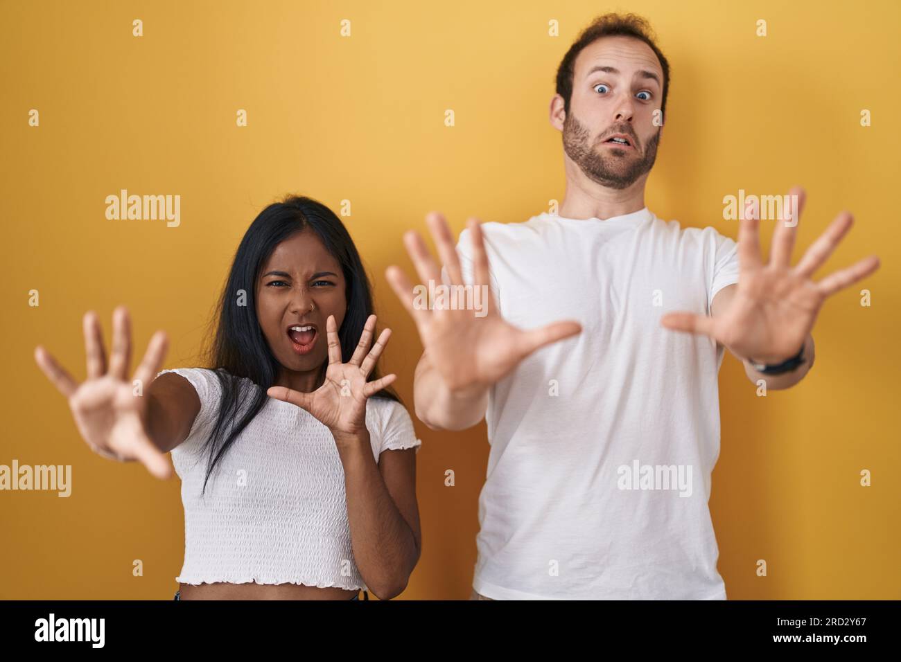 Interracial couple standing over yellow background afraid and terrified ...