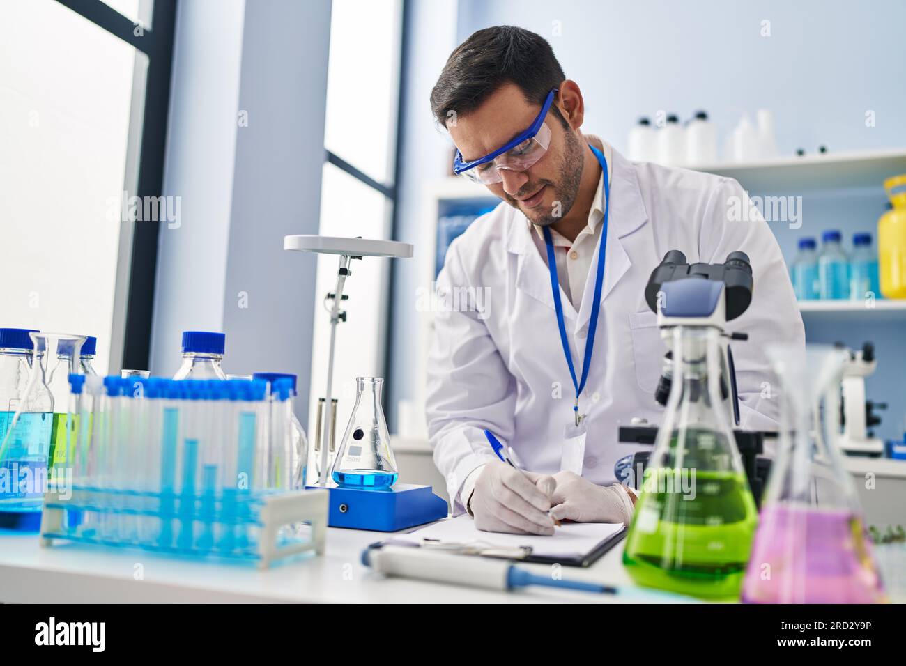Young hispanic man scientist measuring liquid writing report at ...