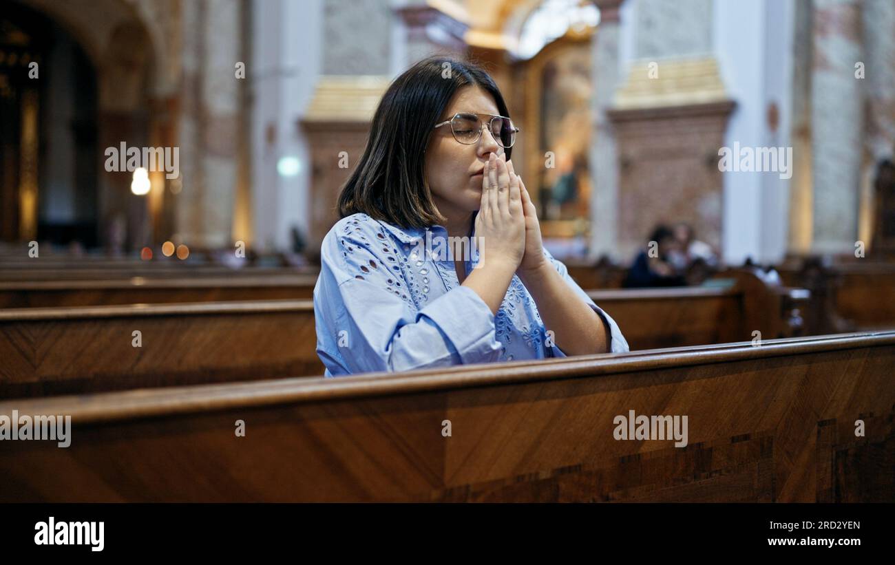 Young beautiful hispanic woman praying on a church bench at St. Karl ...