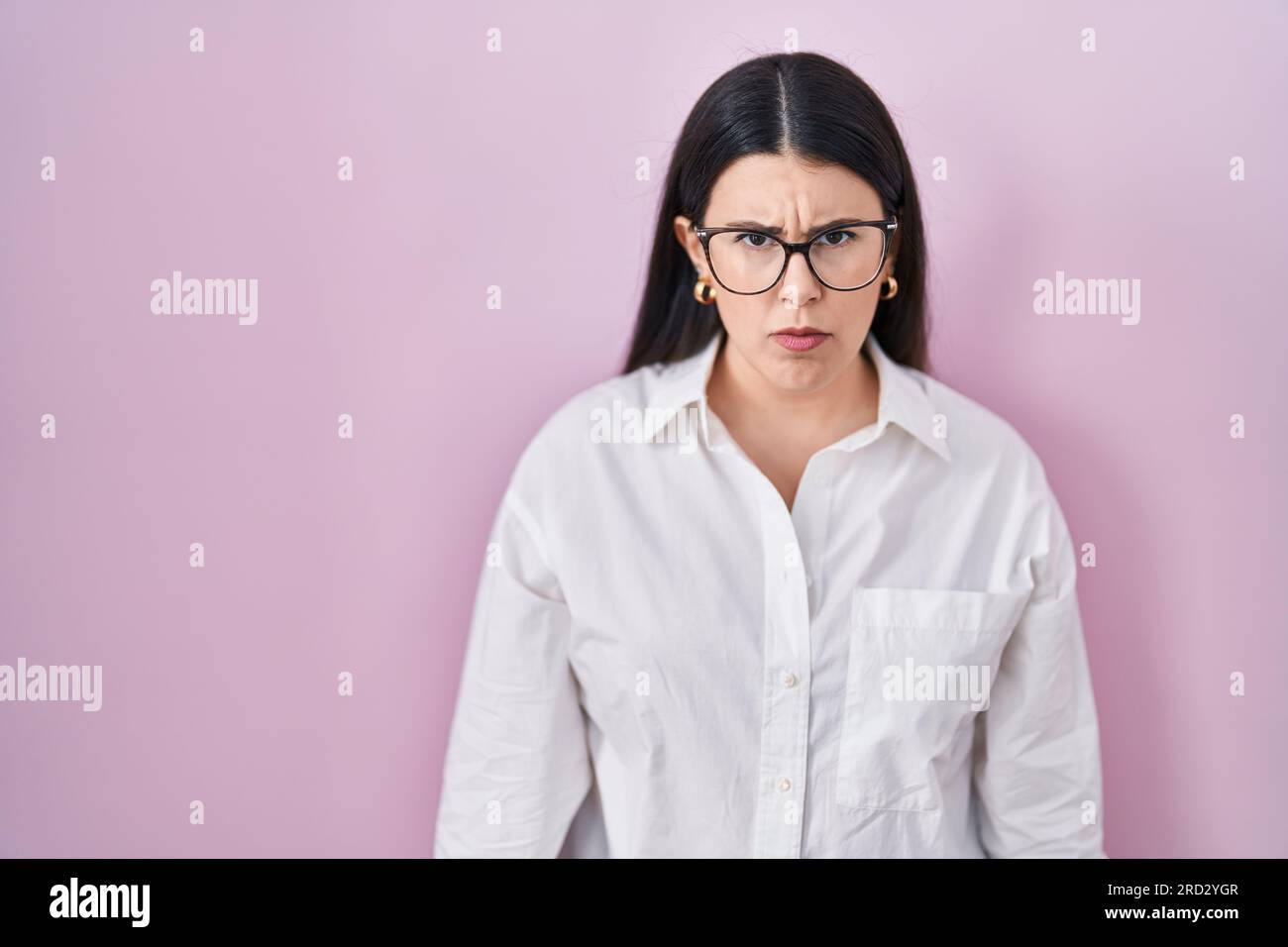 Young brunette woman standing over pink background skeptic and nervous ...