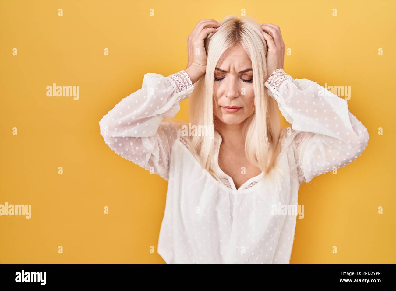 Caucasian woman standing over yellow background suffering from headache ...