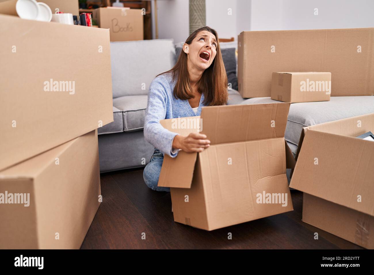Young woman moving to a new home looking inside cardboard box angry and ...