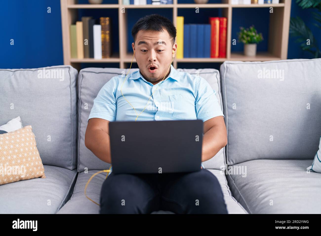 Chinese young man using computer laptop sitting on the sofa scared and ...