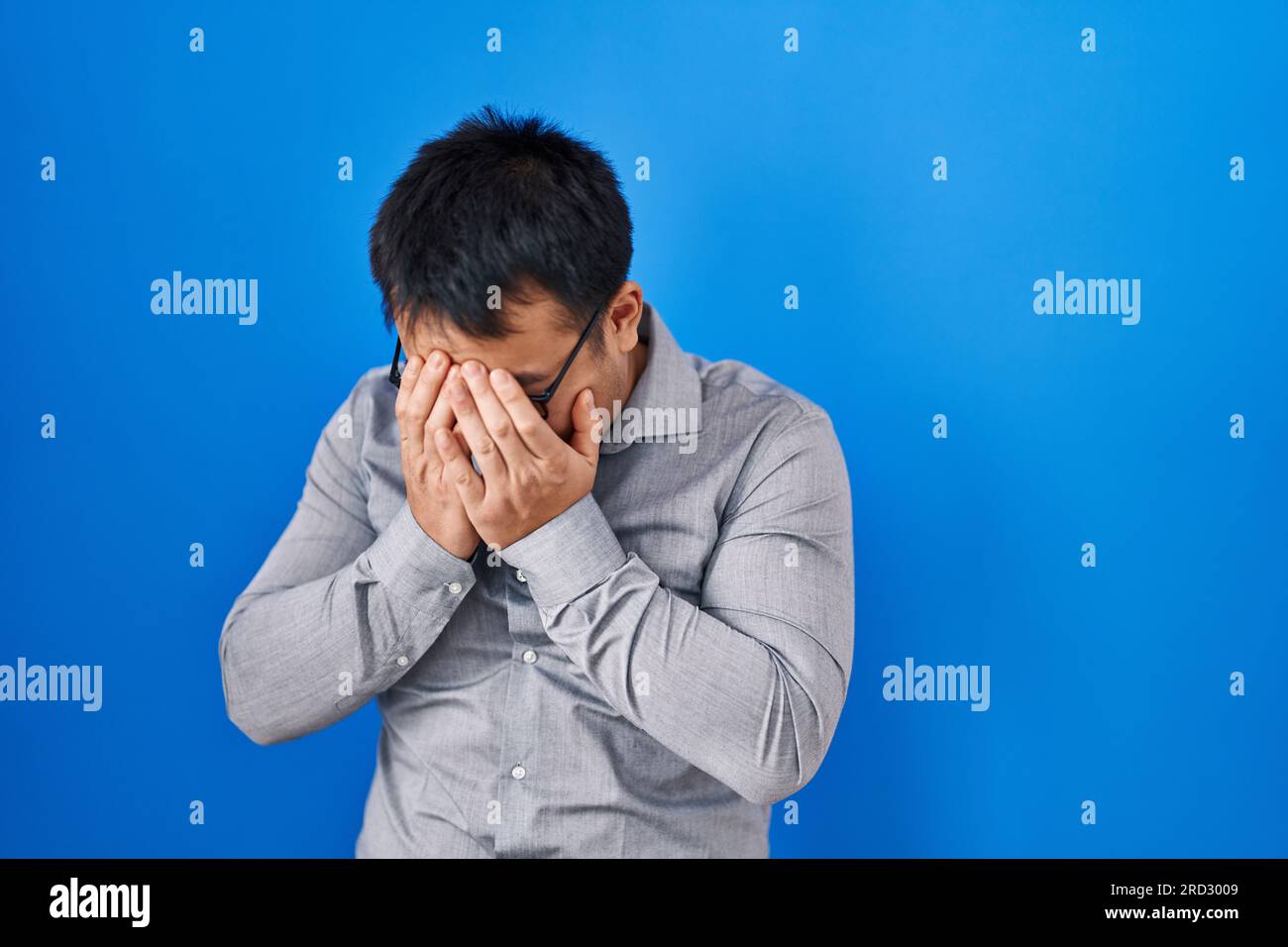 Young chinese man standing over blue background with sad expression ...