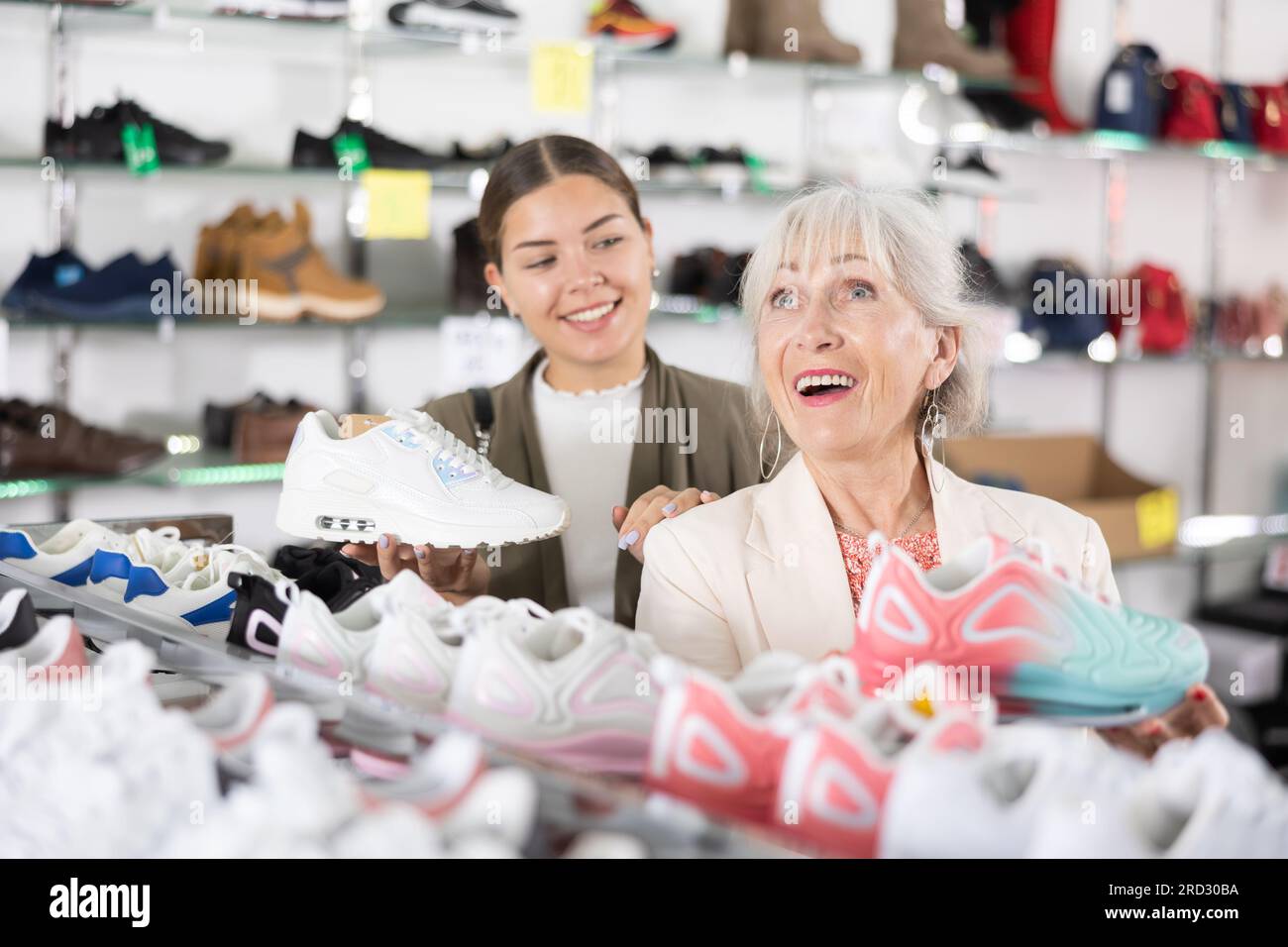 Two positive women of different ages choose new sneakers together in ...