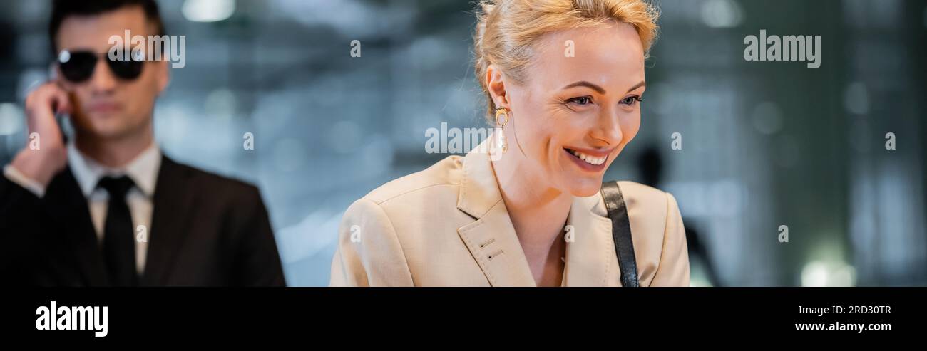 happy blonde woman in formal wear, personal security service concept ...